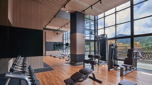 Uma academia com diversos equipamentos de exercício, grandes janelas e vista para uma paisagem montanhosa.