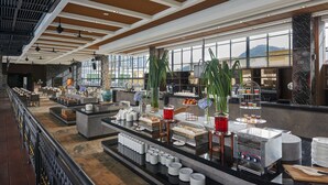 Uma área de buffet com diversos pontos de comida, incluindo uma mesa de frutas e um espaço para bebidas.