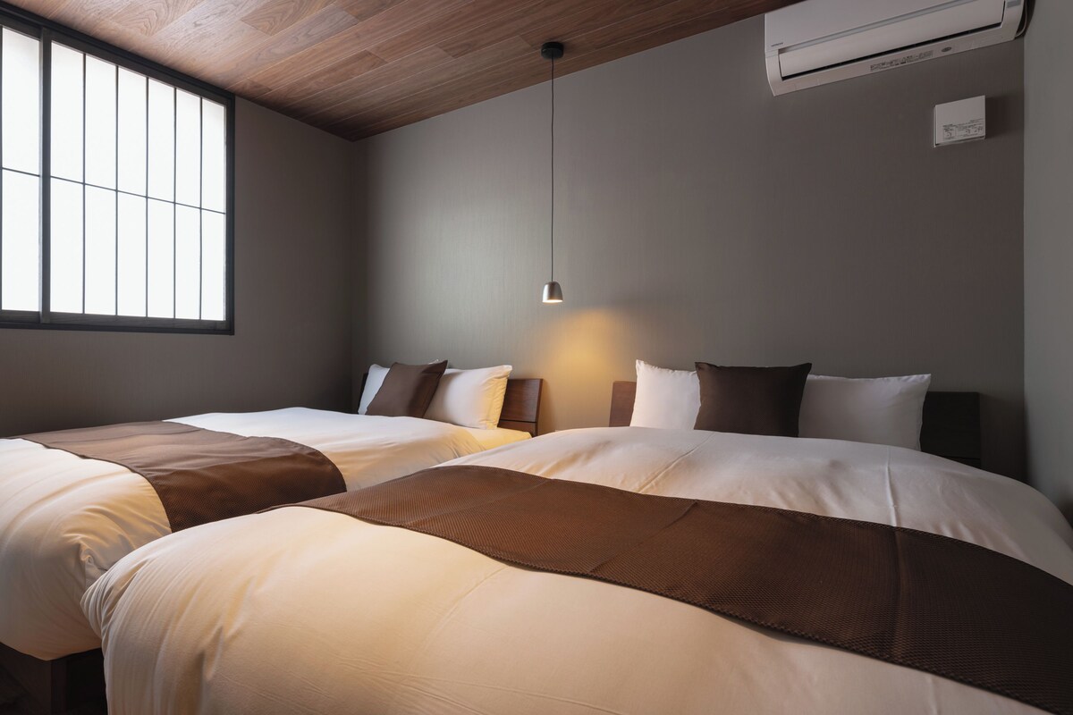 Quarto de hotel com duas camas, uma janela, um ar condicionado e um lustre.