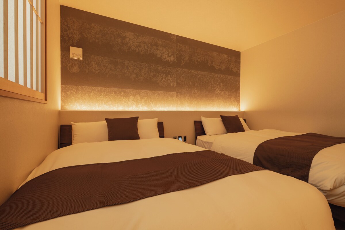 Quarto de hotel com duas camas, uma obra de arte grande na parede e uma mesinha com um telefone.