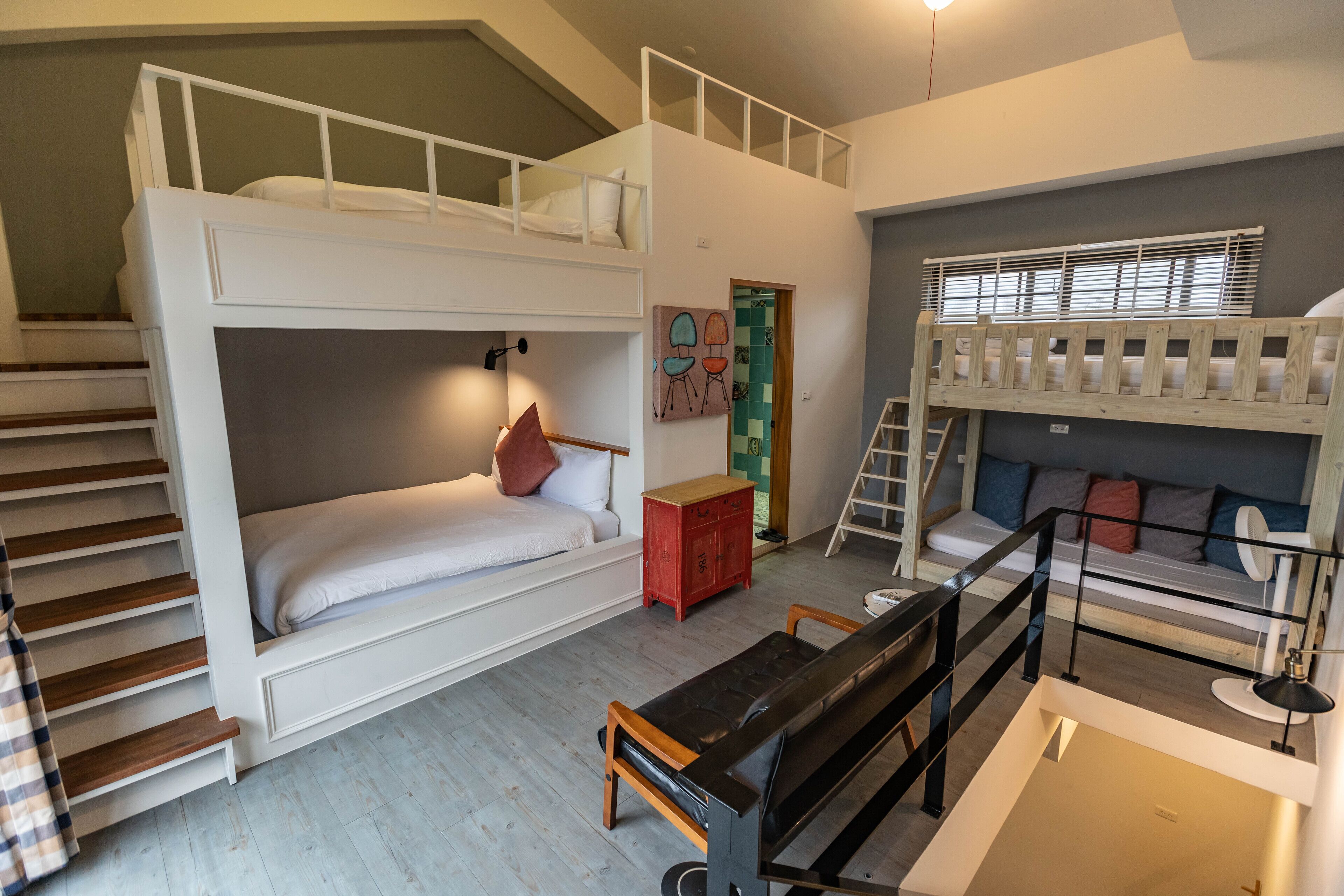 Quarto com beliche de vários níveis, escada, mesa pequena e um banco.
