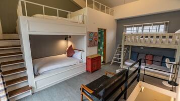 Quarto com beliche de vários níveis, escada, mesa pequena e um banco.