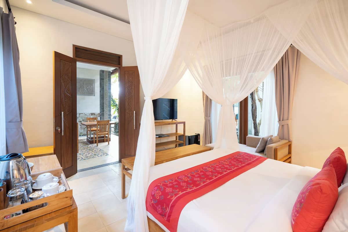 Quarto de hotel com cama, televisão, mesa de madeira com cafeteira e porta que dá para uma varanda.