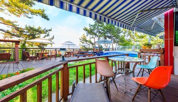 Um terraço ao ar livre com mesas e cadeiras de madeira, guarda-sóis e área de piscina.