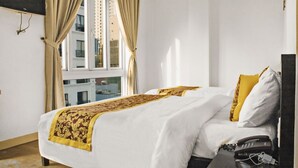 Quarto de hotel com uma cama, mesa de cabeceira, telefone e janela com cortinas.