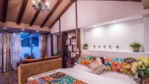 Quarto com teto de madeira, cama com roupa de cama floral colorida, cabeceira de vime e mesa de cabeceira com uma planta.