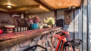 Uma área de bar com balcão de pedra, banquetas vermelhas e diversos objetos decorativos.