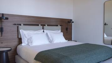 Cama bem arrumada com lençóis brancos e manta verde, cabeceira de madeira e abajures laterais.