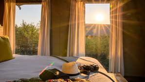 Uma cama com uma manta estampada, um chapéu, uma câmera e um smartphone.