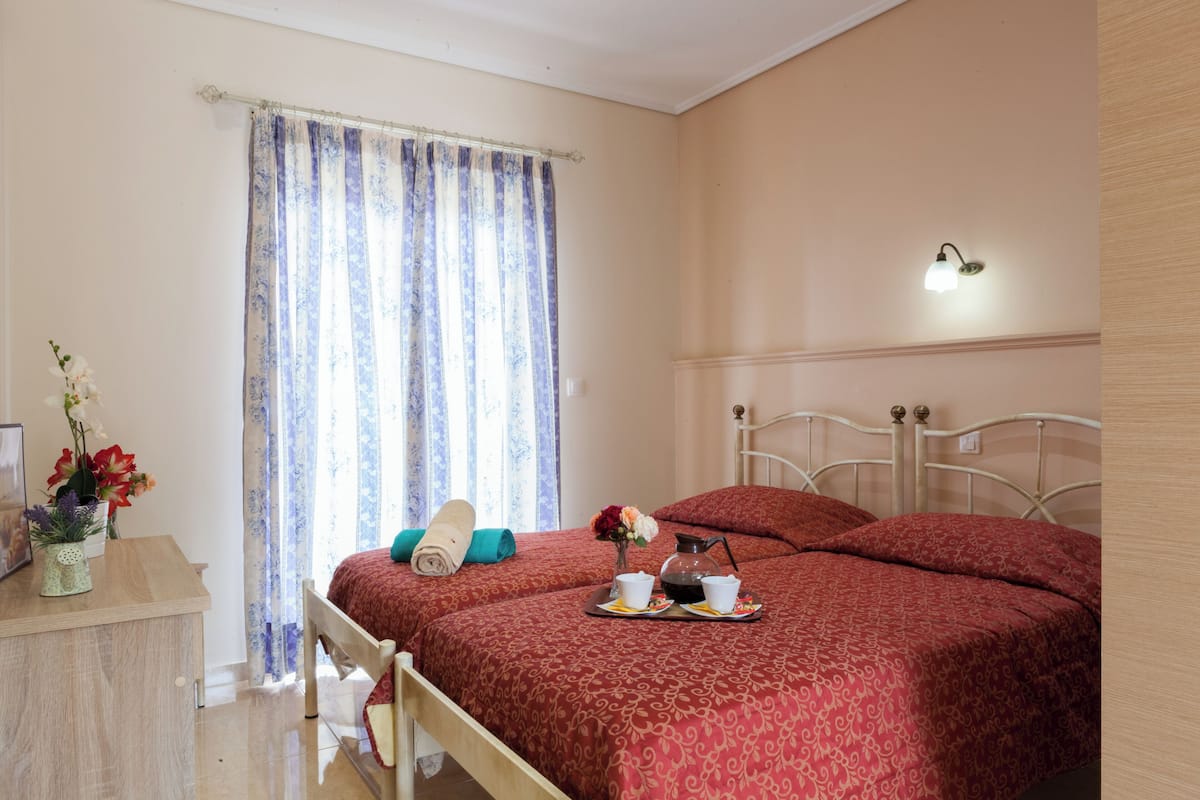 Quarto com cama, mesa de cabeceira, luminária e janela com cortinas.