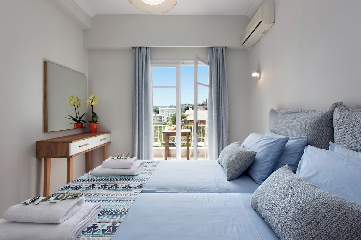 Quarto moderno com uma cama grande, mesa de cabeceira com espelho e vista para o exterior através de uma porta de correr.