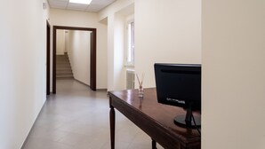 Um corredor com uma escrivaninha de madeira, um monitor de computador e um vaso com raminhos de cana.