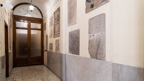 Um corredor com piso de mármore, porta de madeira com painéis de vidro e parede com placas e um relógio.