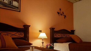 Quarto de hotel com duas camas, uma mesa de cabeceira com abajur e luminária na parede.