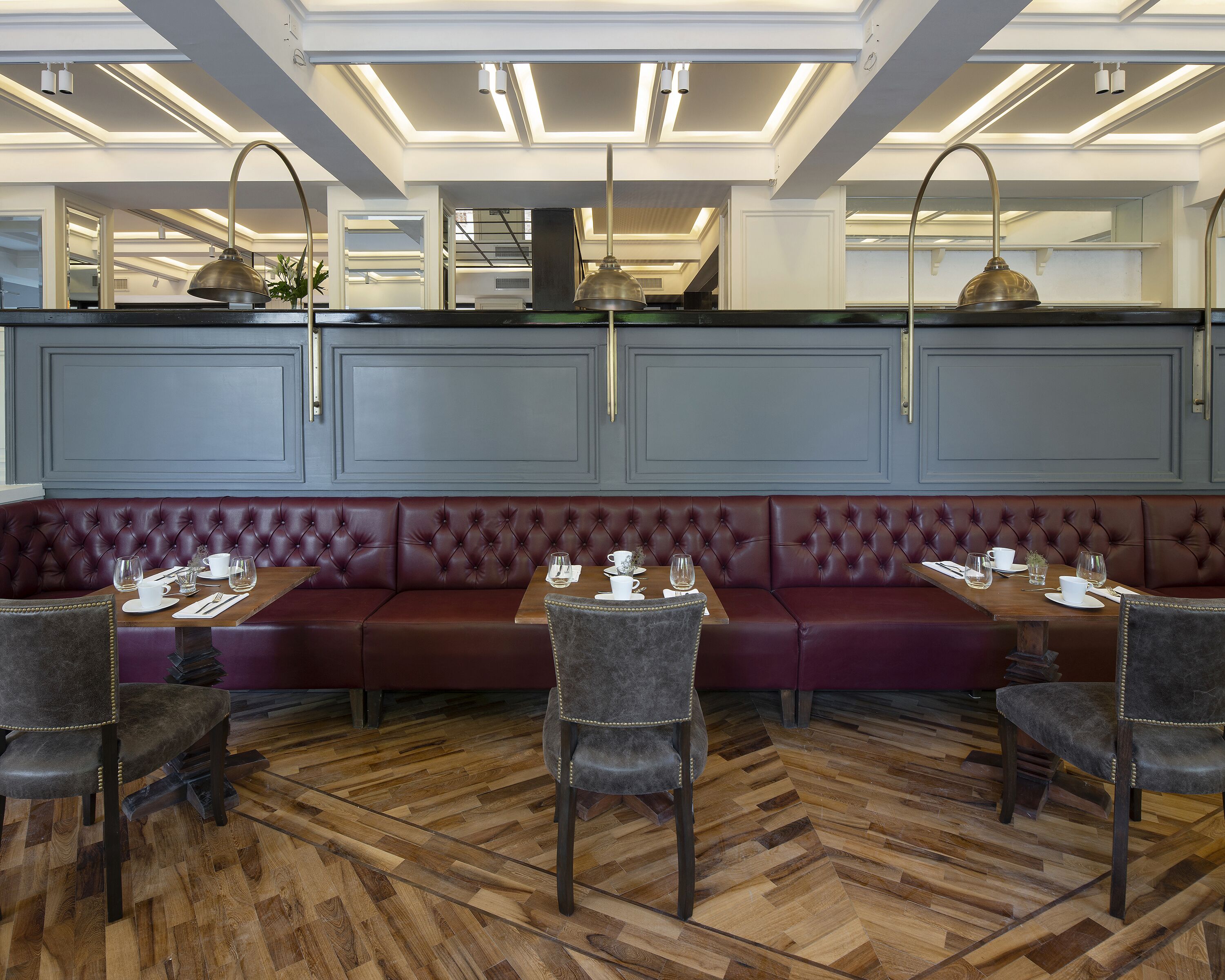 Um restaurante com piso de madeira em padrão espinha de peixe, assento de couro marrom e mesa de madeira com pratos e copos brancos.