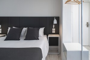 Quarto moderno com uma cama grande, duas mesas de cabeceira, um criado-mudo e um cabideiro.