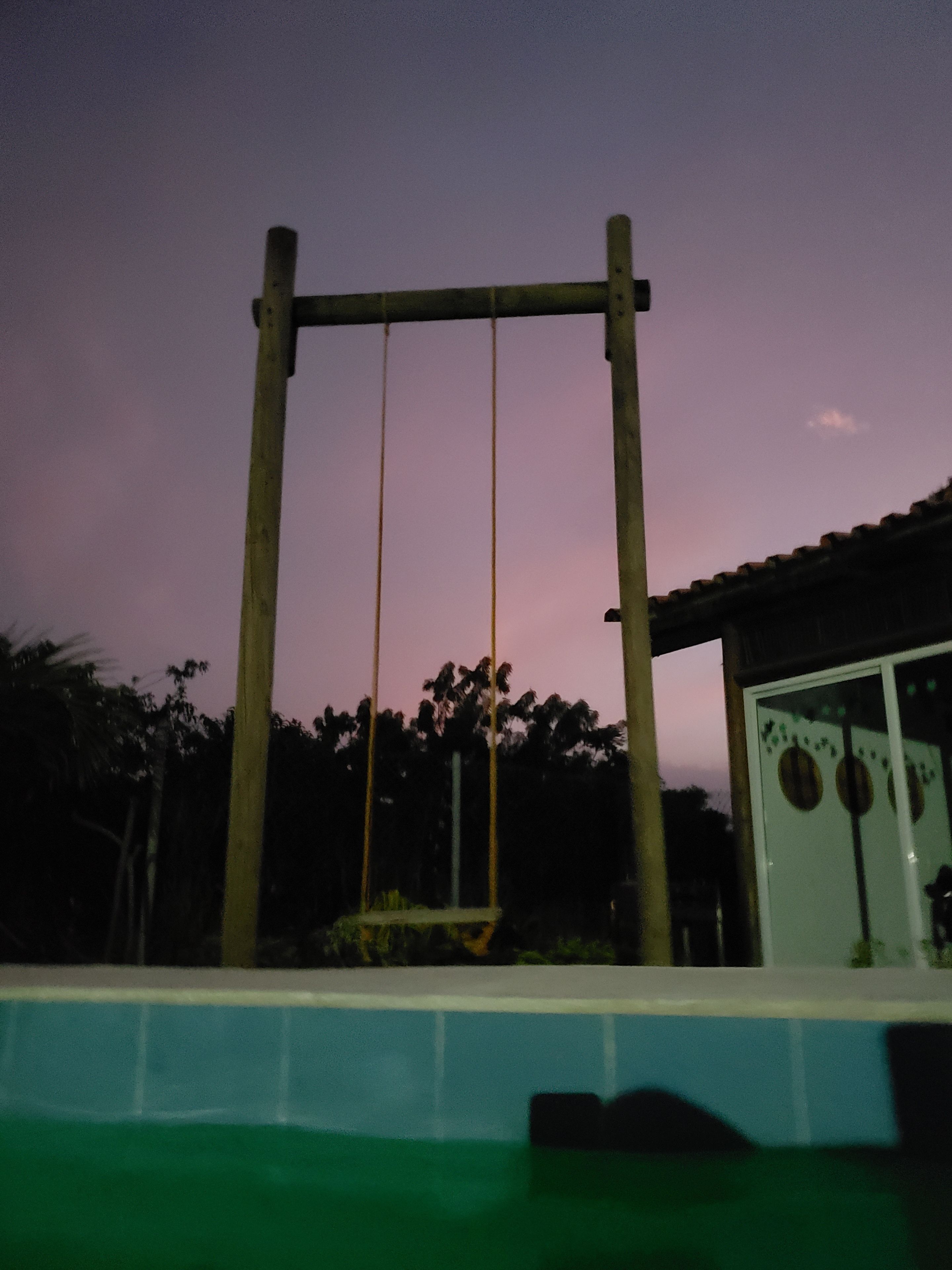 Um baloiço sobre uma piscina, com um edifício ao fundo.