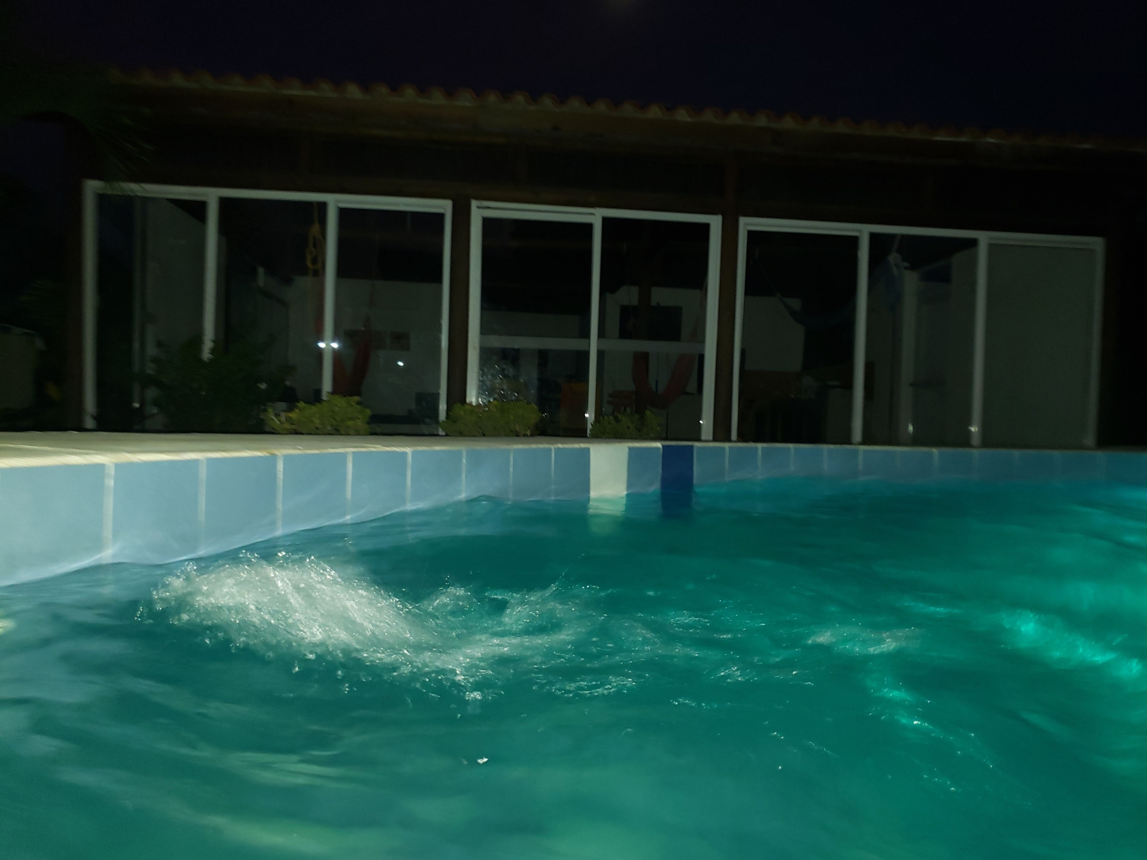 Piscina  à noite com água cristalina, rodeada por um edifício com grandes janelas.