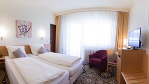 Quarto de hotel com duas camas, uma escrivaninha, uma cadeira, uma televisão e um quadro na parede.