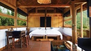 Quarto de madeira com cama, uma mesinha e luminária pendente.