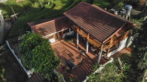 Uma casa de dois andares com telhado de telhas, rodeada por vegetação exuberante e campos em socalcos.