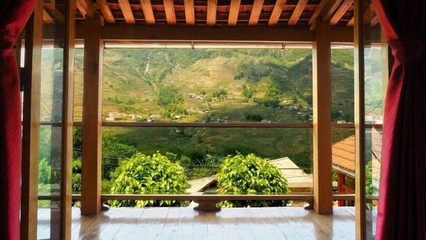 Quarto com teto de madeira e janelas amplas que dão para um vale verde.