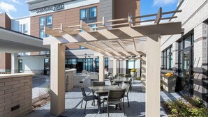 Pátio de hotel com mobiliário ao ar livre, pérgola e placa da Marriott.