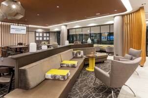 Um hall de hotel moderno com uma mesa de recepção, área de estar e uma grande janela com vista para a cidade.