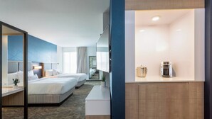 Quarto de hotel com uma cama grande, uma cama menor, uma escrivaninha e uma máquina de café.
