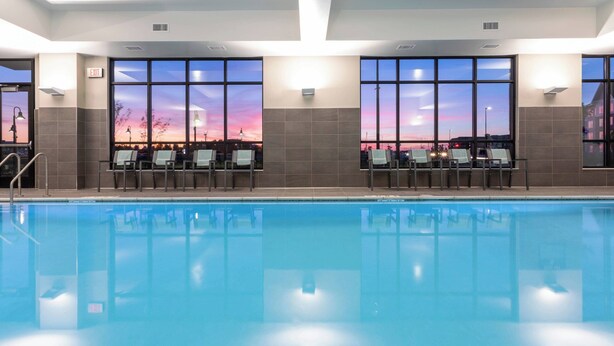 Piscina com cadeiras e mesas, grandes janelas com vista para o pôr do sol e uma placa de saída.