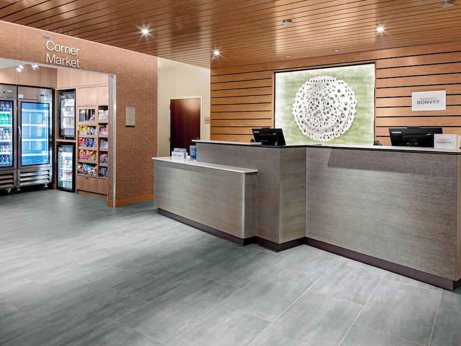 Uma área de recepção de hotel com uma loja de conveniência no canto, um computador Lenovo e um grande painel decorativo.