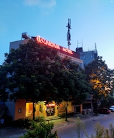 Um hotel com um letreiro de neon chamativo, entrada visível e vegetação ao redor.