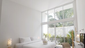 Quarto moderno com uma cama grande, uma escrivaninha com computador e vista para o verde através de uma janela ampla.