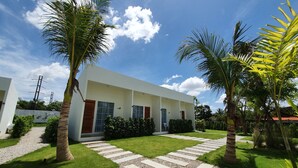 Um edifício moderno com fachada branca, um caminho pavimentado e palmeiras.