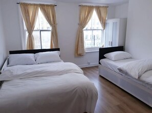 Quarto com duas camas, um guarda-roupa e uma janela com cortinas.