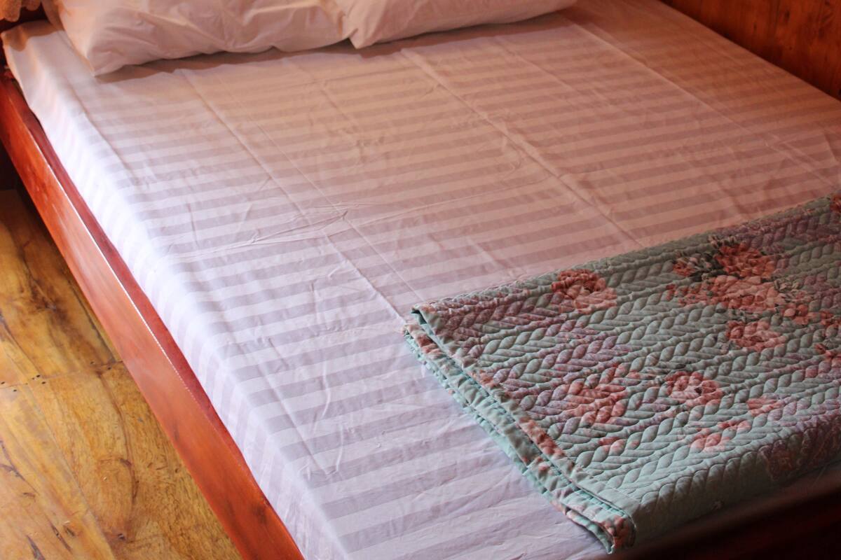 Uma cama de madeira com roupa de cama branca e um edredom.