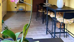 Um quarto de paredes amarelas com uma mesa de jantar, cadeiras, um vaso de plantas, um candeeiro suspenso e um relógio na parede.