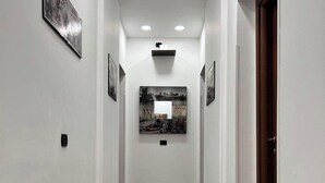 Um corredor moderno com chão de madeira, paredes brancas e quadros emoldurados.