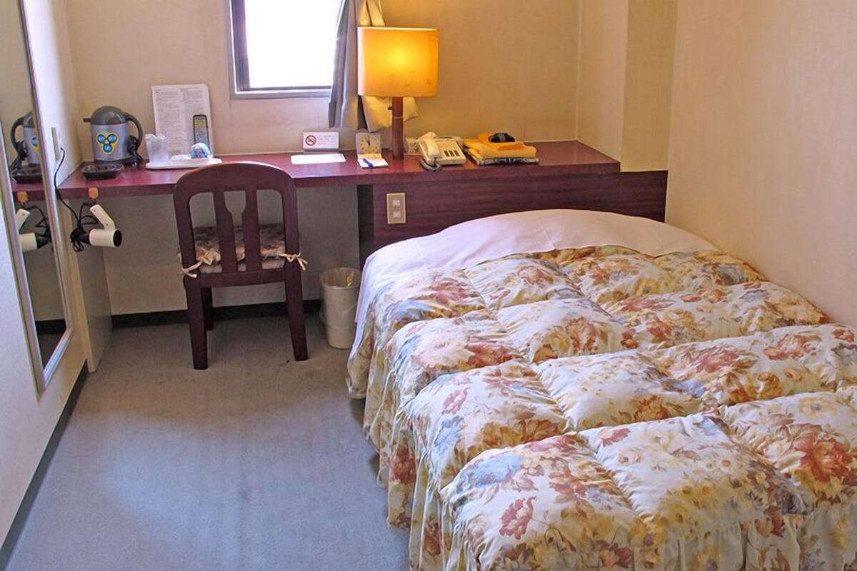 Quarto com escrivaninha, cadeira, luminária e edredom estampado com flores.