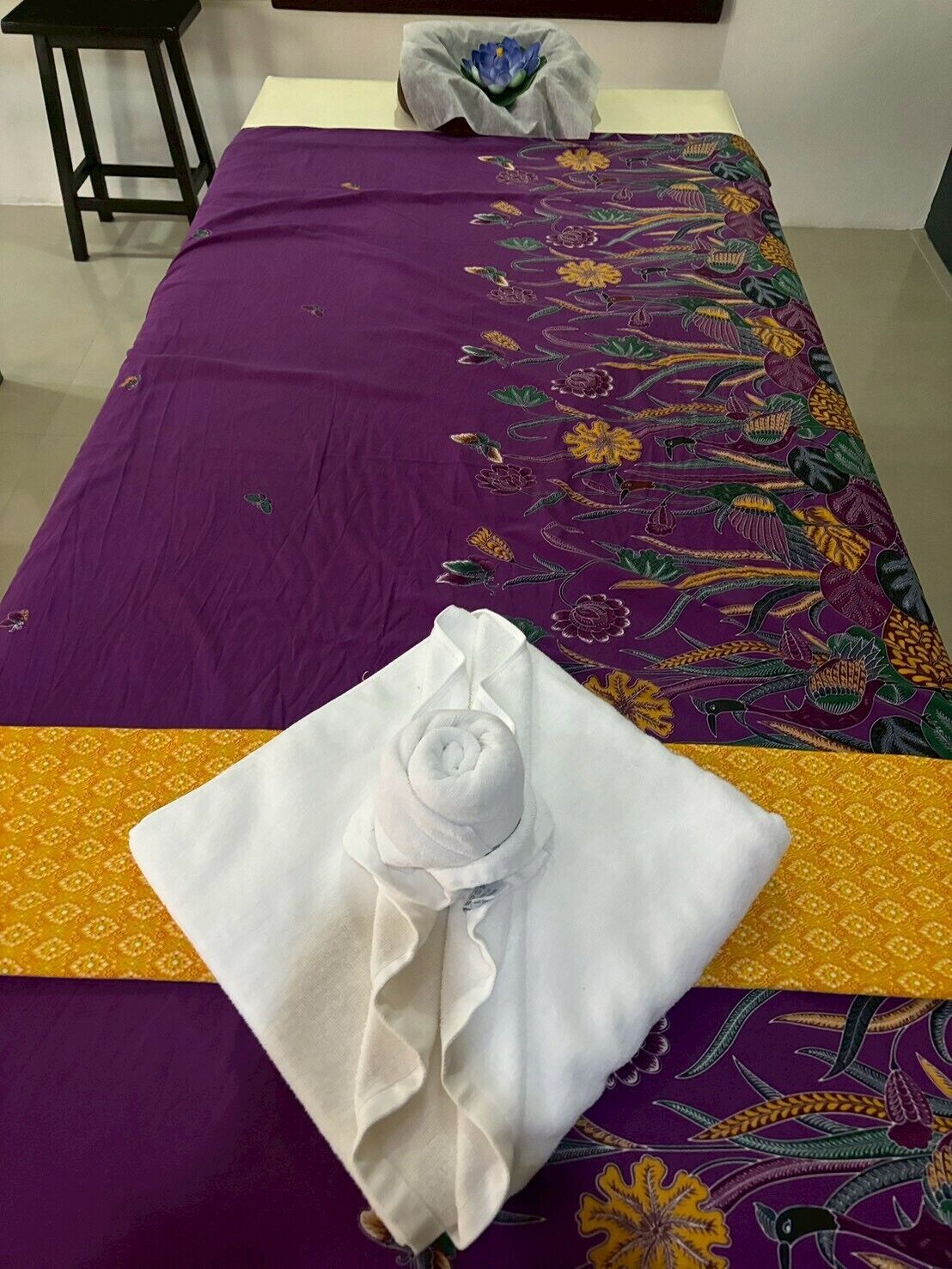 Cama com colcha roxa e toalha branca dobrada.