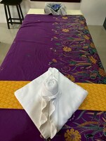 Cama com colcha roxa e toalha branca dobrada.