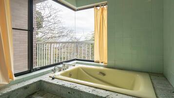 Um banheiro com banheira, janela com vista e varanda com guarda-corpo.