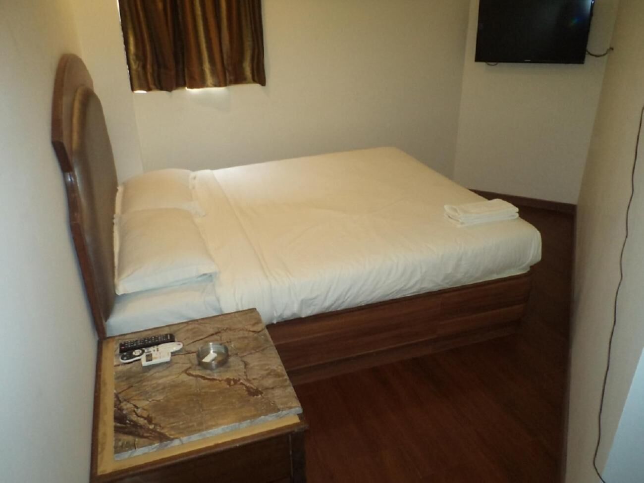 Uma cama pequena e bem arrumada com lençóis brancos num quarto compacto.