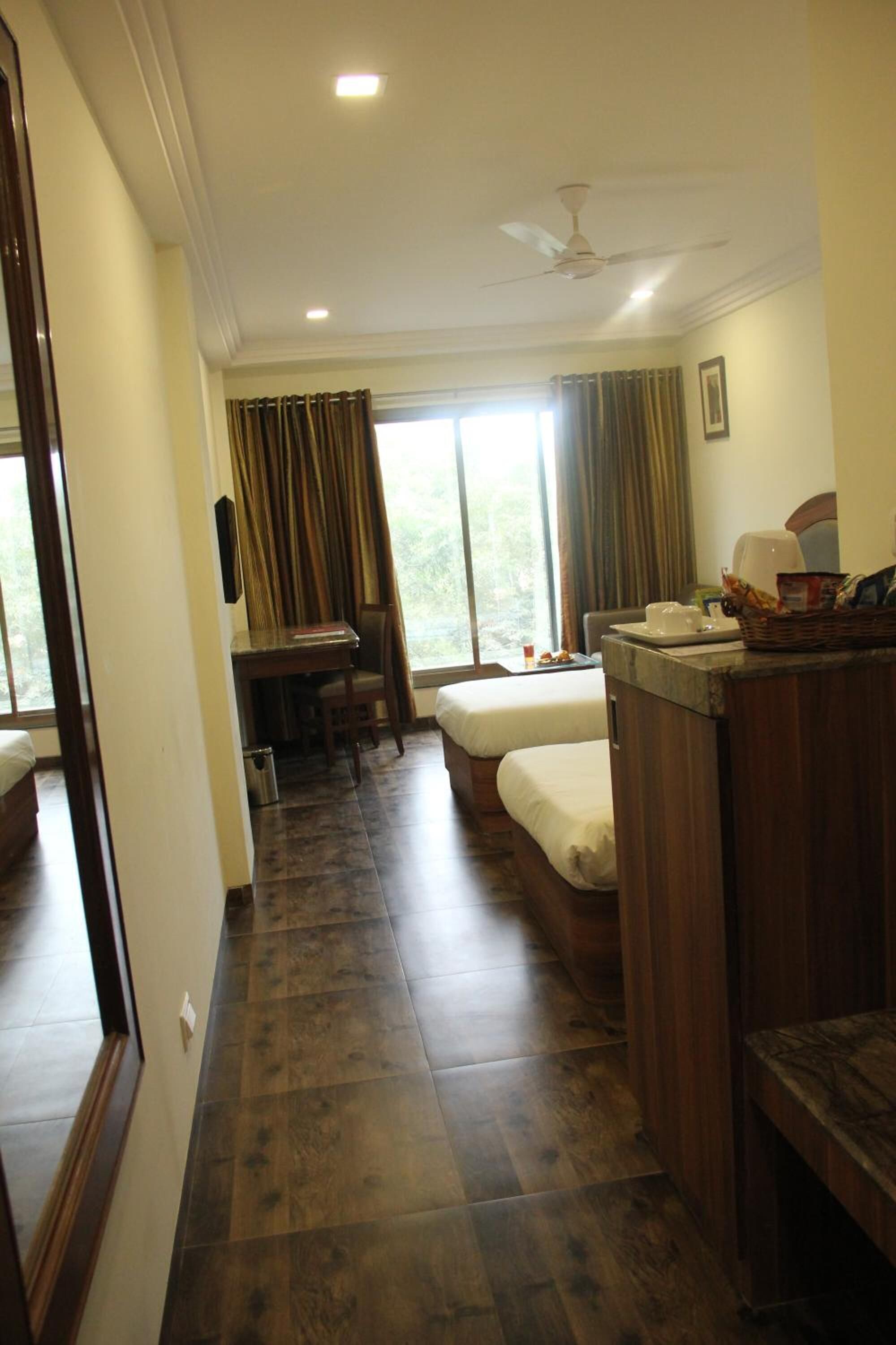 Quarto de hotel com duas camas, uma escrivaninha, uma cadeira, uma mesinha e uma janela com cortinas.