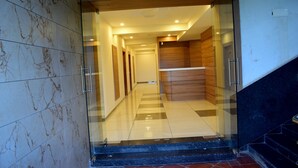 Um lobby de hotel moderno com entrada de vidro, paredes de mármore e um balcão de recepção de madeira.