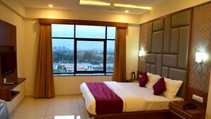 Quarto de hotel com uma cama grande, televisão, mesa de cabeceira e janela com cortinas.