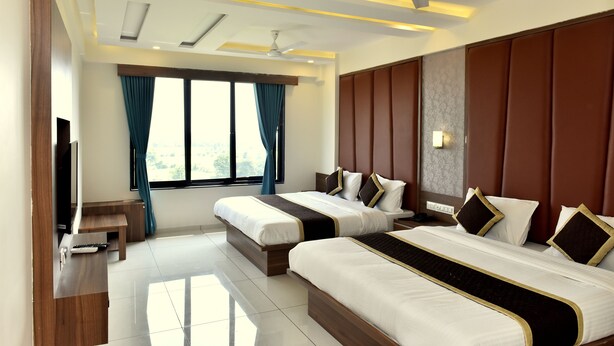 Quarto de hotel com duas camas, uma escrivaninha, televisão e janela com cortinas.
