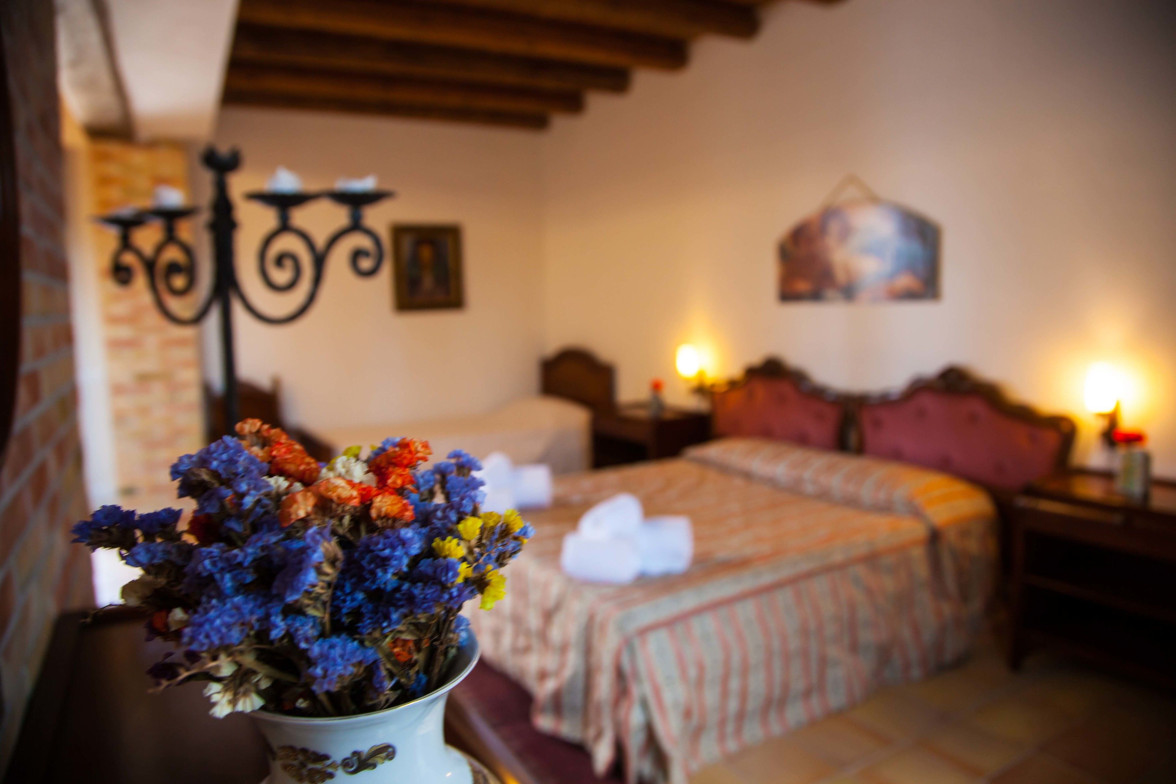 Quarto com cama, mesa de cabeceira, abajur e um vaso de flores.