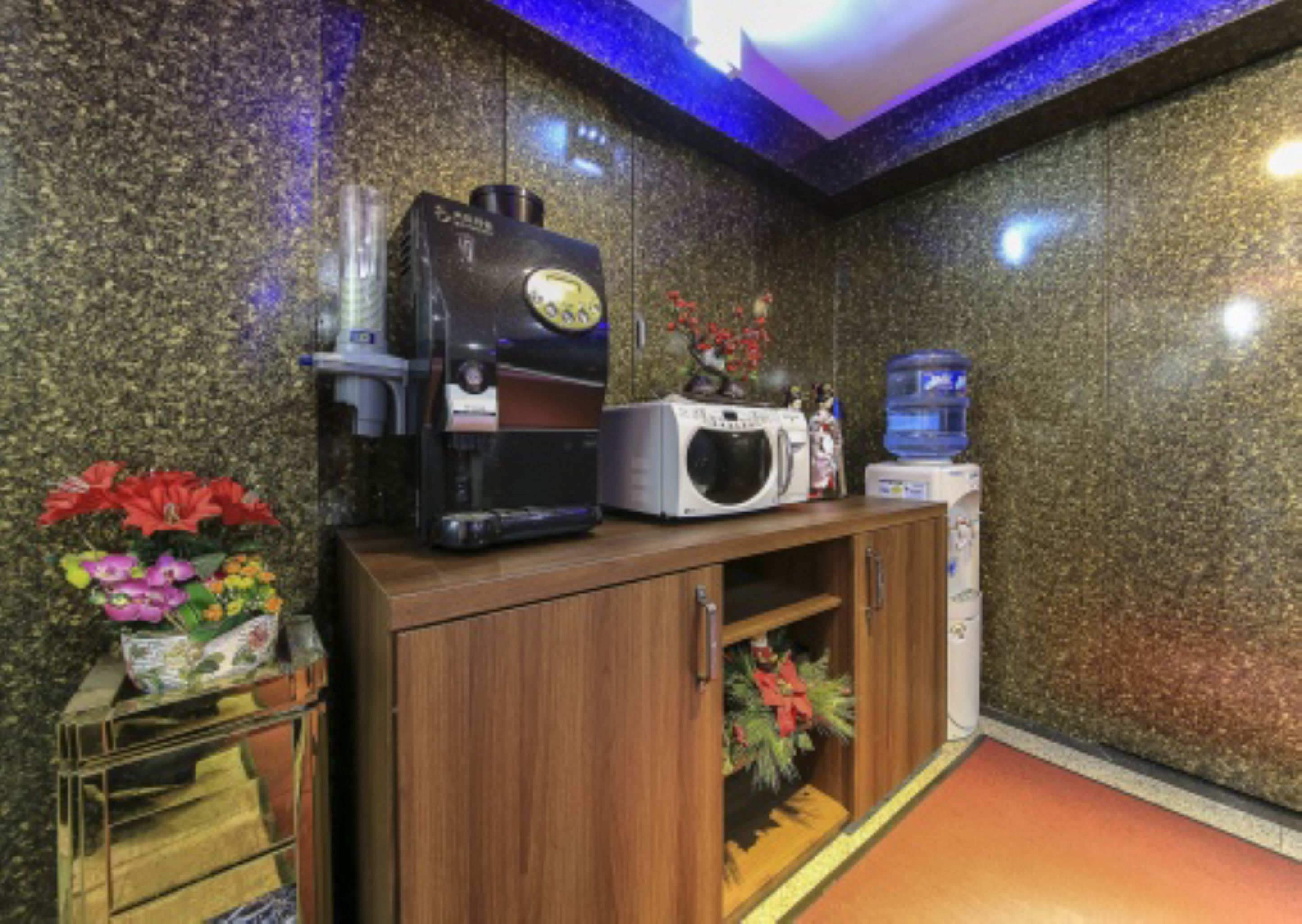 Uma área de cozinha compacta com máquina de café, micro-ondas e dispensador de água, tudo sobre um armário de madeira.