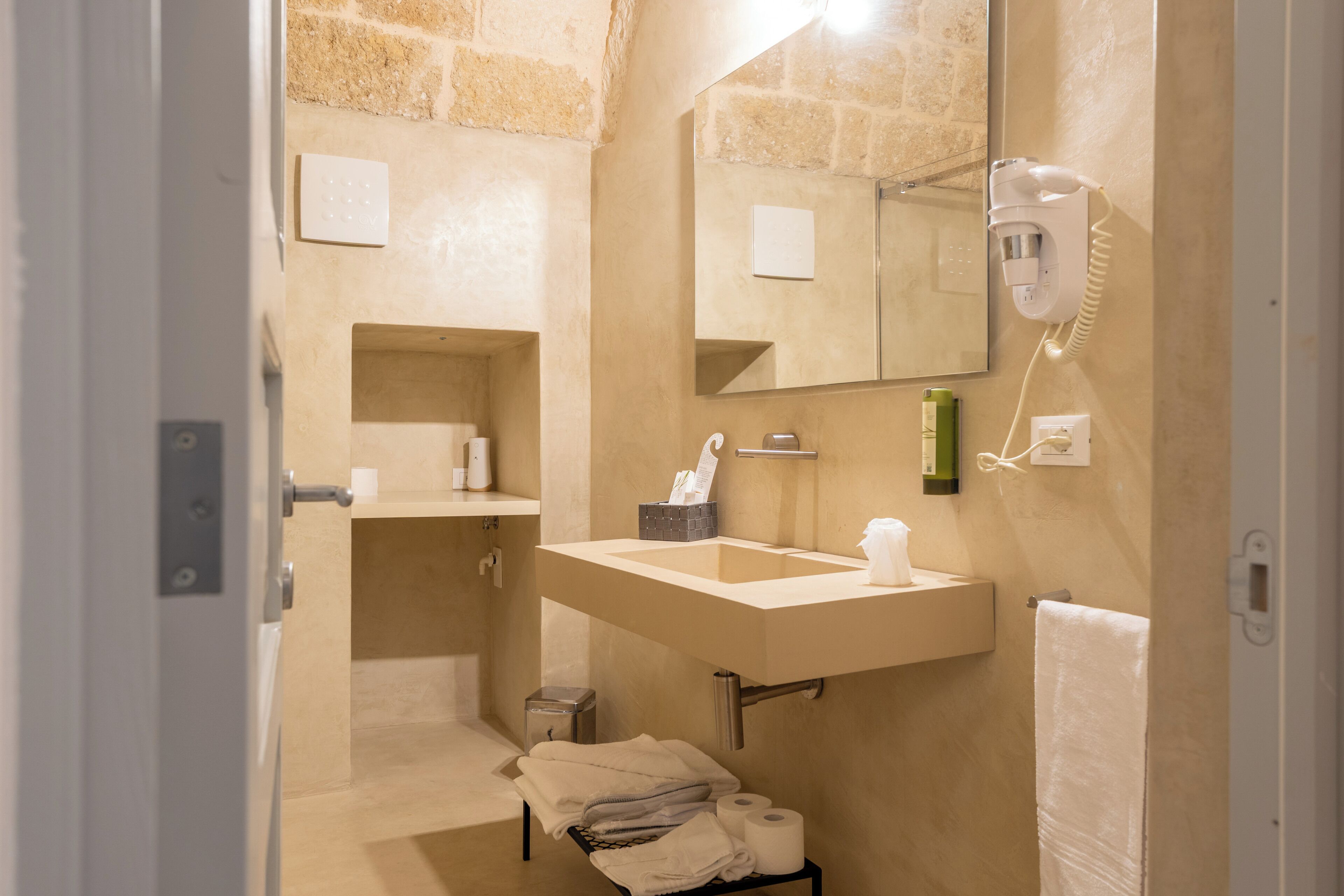 Casa de banho com lavatório bege, espelho, secador de cabelo e porta-toalhas.